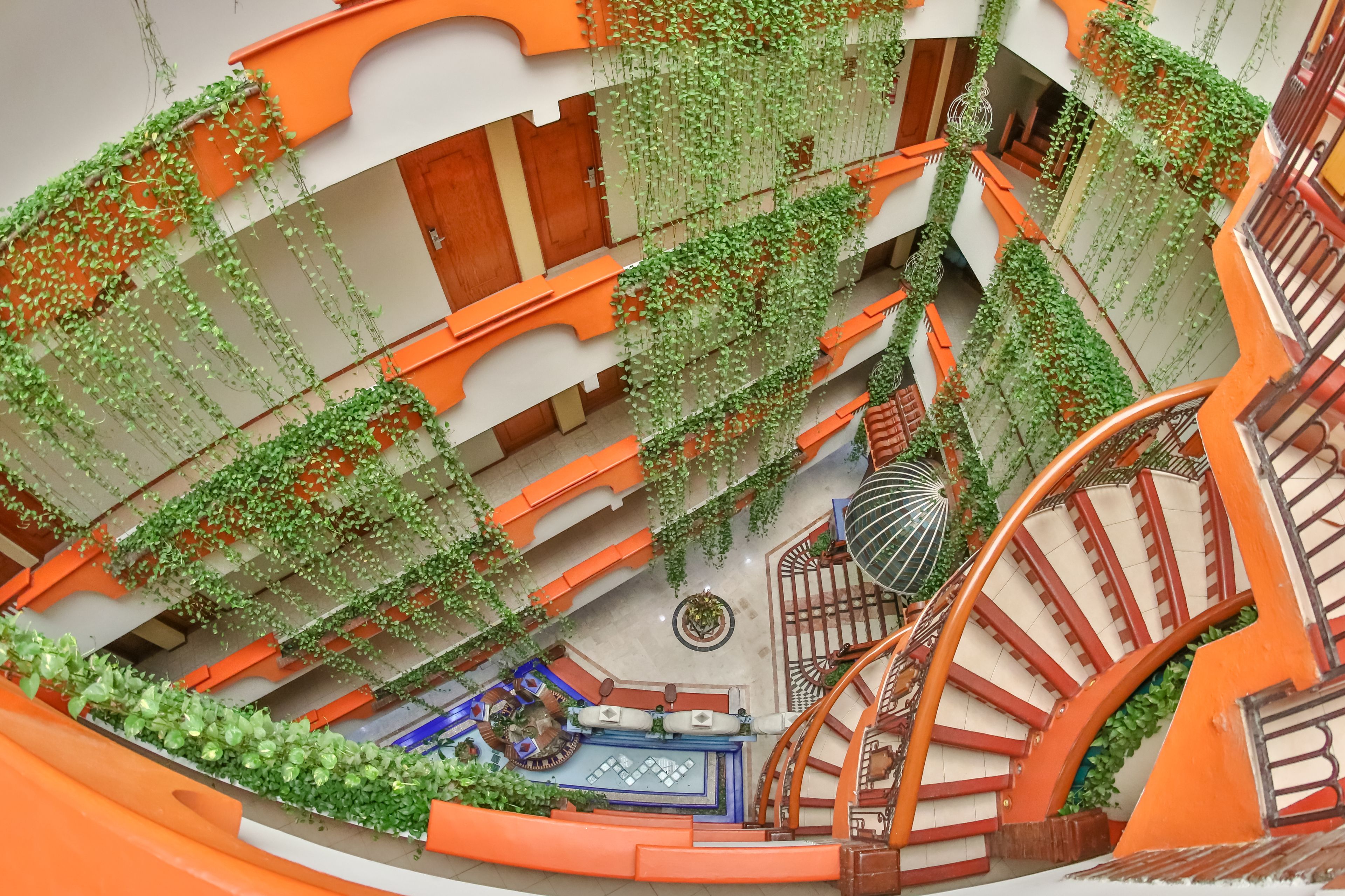 Um átrio com vários níveis, com guarda-corpos laranja, plantas verdes e uma escadaria em espiral central.