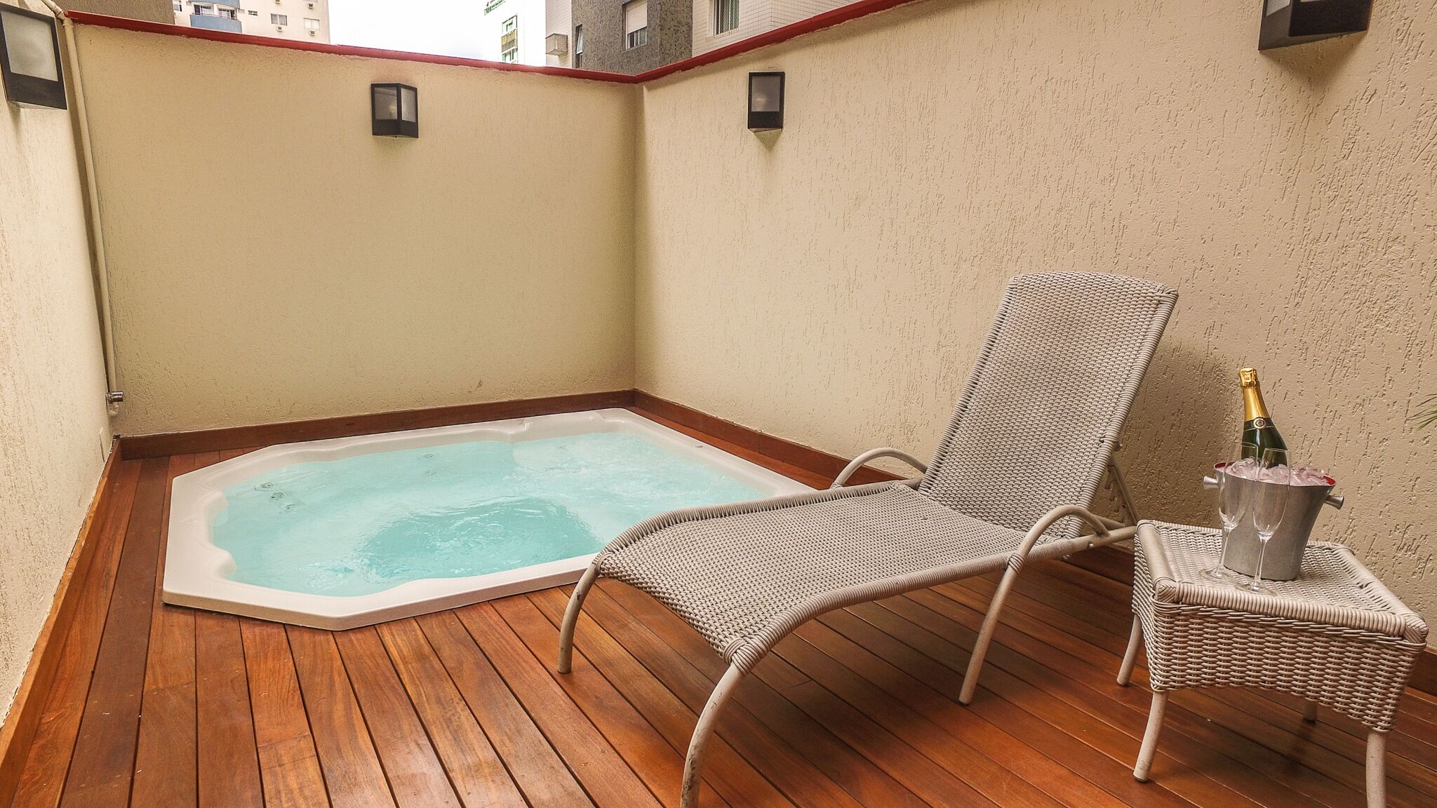 Uma banheira de hidromassagem com uma cadeira de vime e uma mesa pequena com uma garrafa e copos.