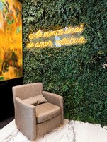 Um quarto com uma parede coberta de folhagem verde, uma poltrona bege e um quadro.