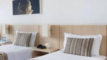 Quarto de hotel com duas camas, cada uma com cabeceira e mesas de cabeceira. Há um quadro emoldurado na parede acima das camas.