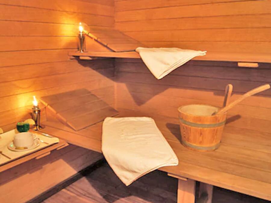 Uma sala de sauna com paredes de madeira, um banco, uma toalha, um balde e duas velas acesas.