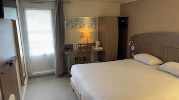 Quarto de hotel com cama, escrivaninha com luminária, guarda-roupa e porta que dá para uma varanda.
