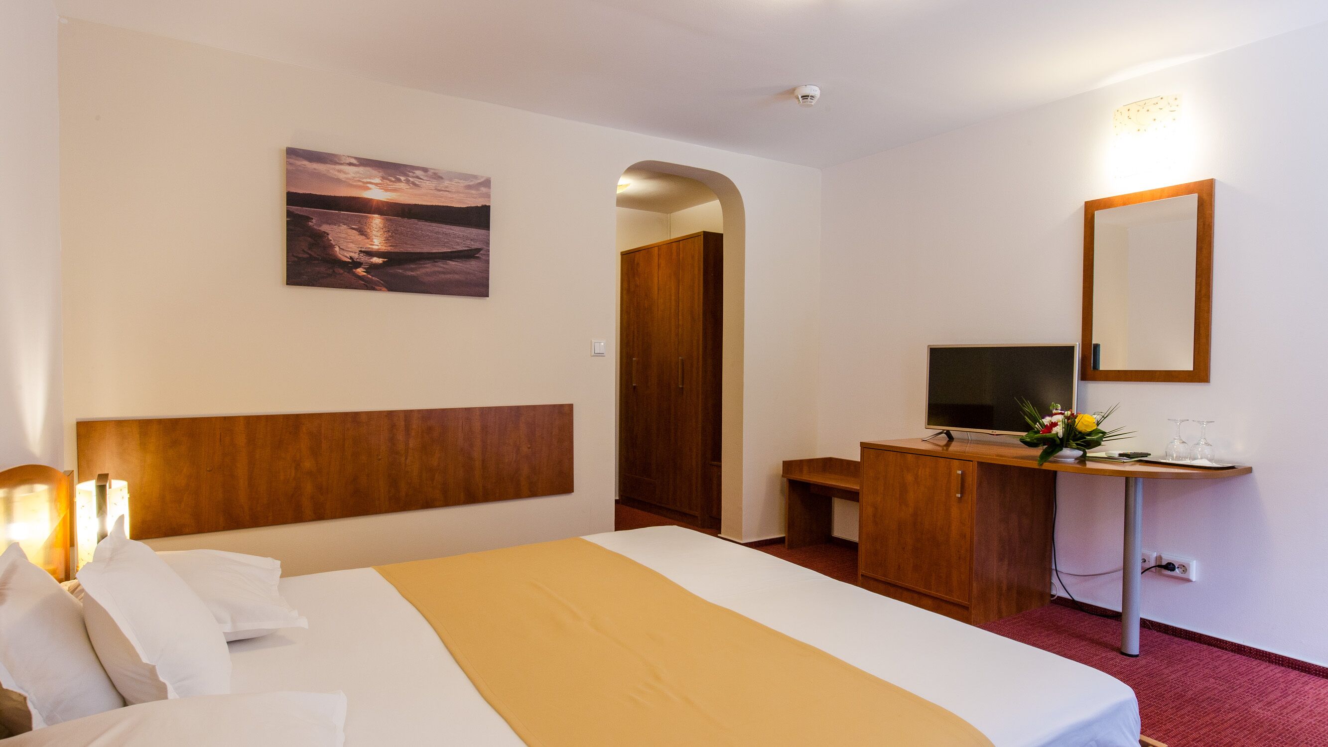 Quarto de hotel com cama, escrivaninha, televisão e espelho.