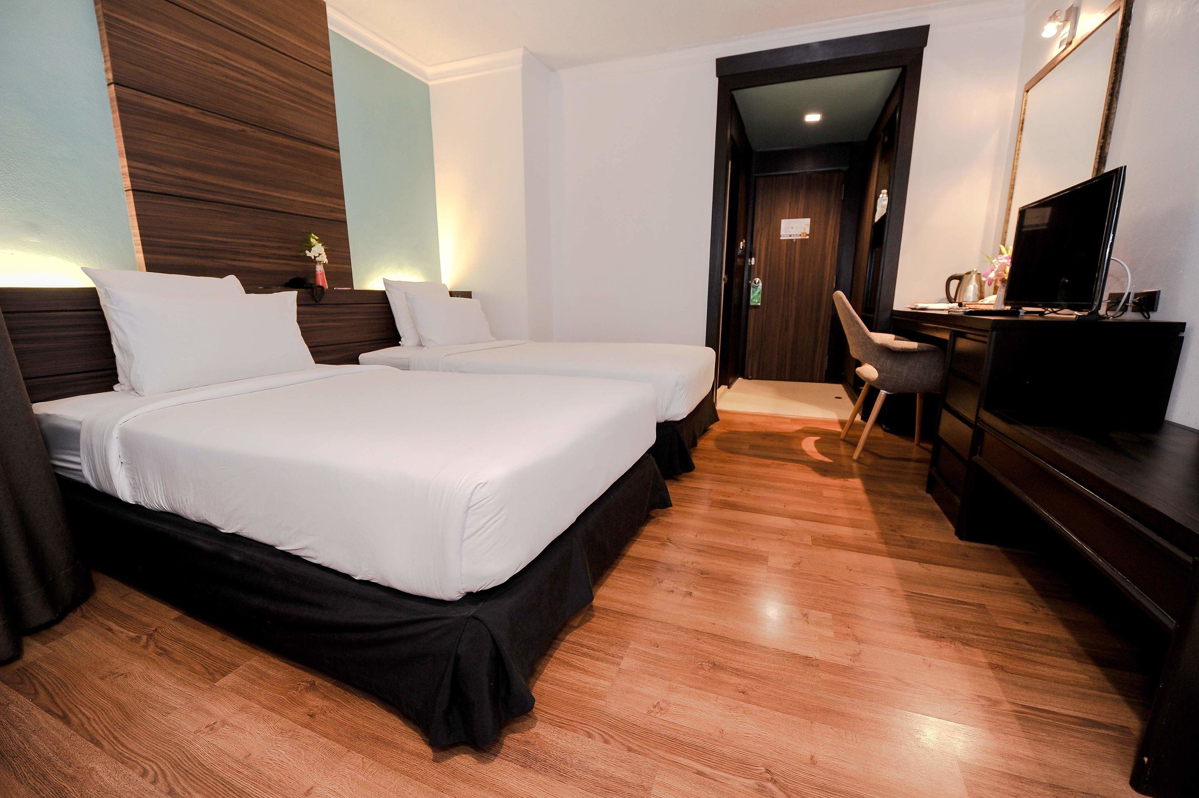 Quarto de hotel com duas camas, uma escrivaninha, uma cadeira e uma televisão.