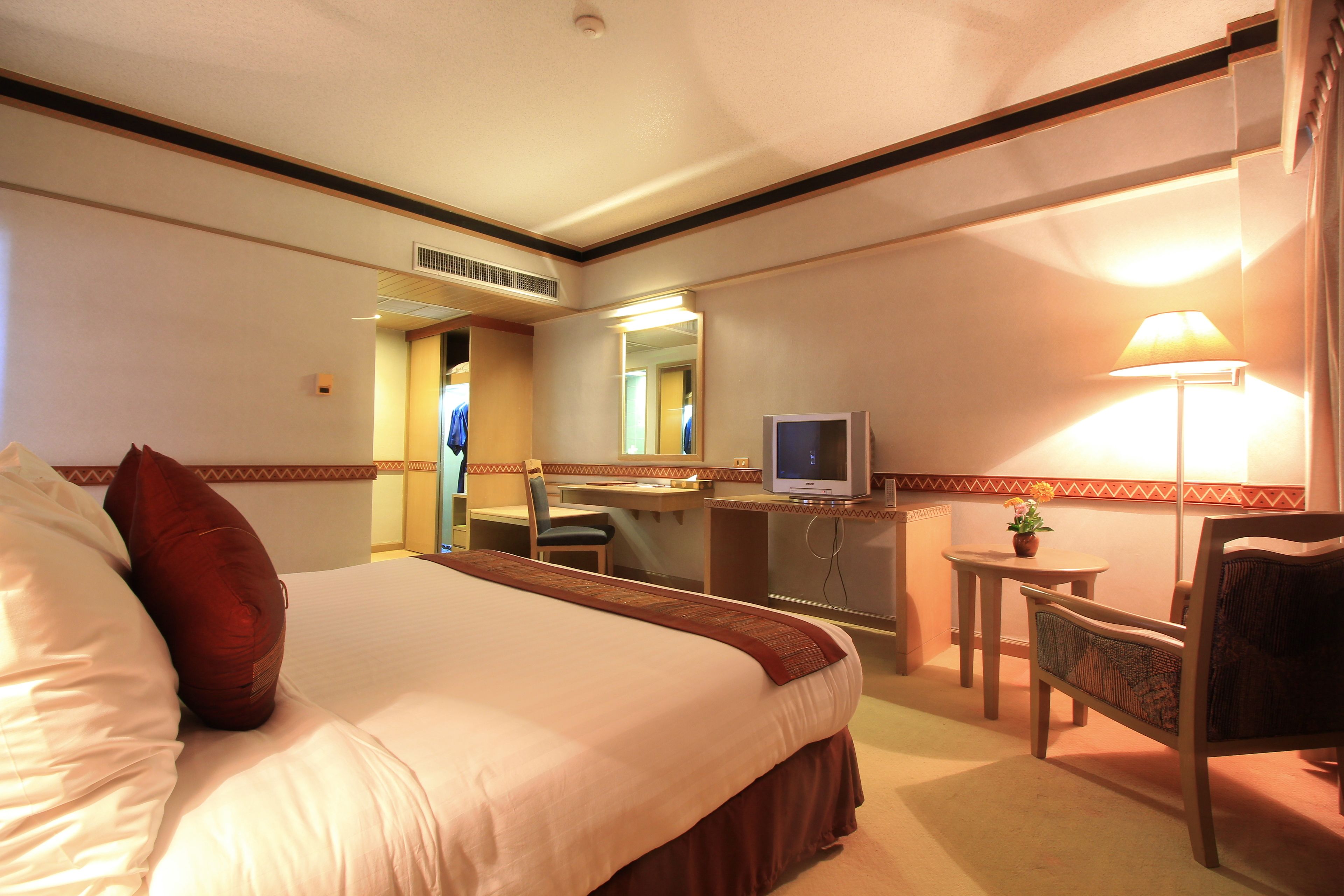 Quarto de hotel com uma cama grande, escrivaninha, cadeira, televisão e abajur.