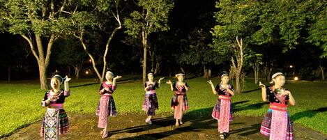 Um grupo de pessoas vestindo trajes tradicionais se apresenta em um caminho pavimentado em um parque à noite.