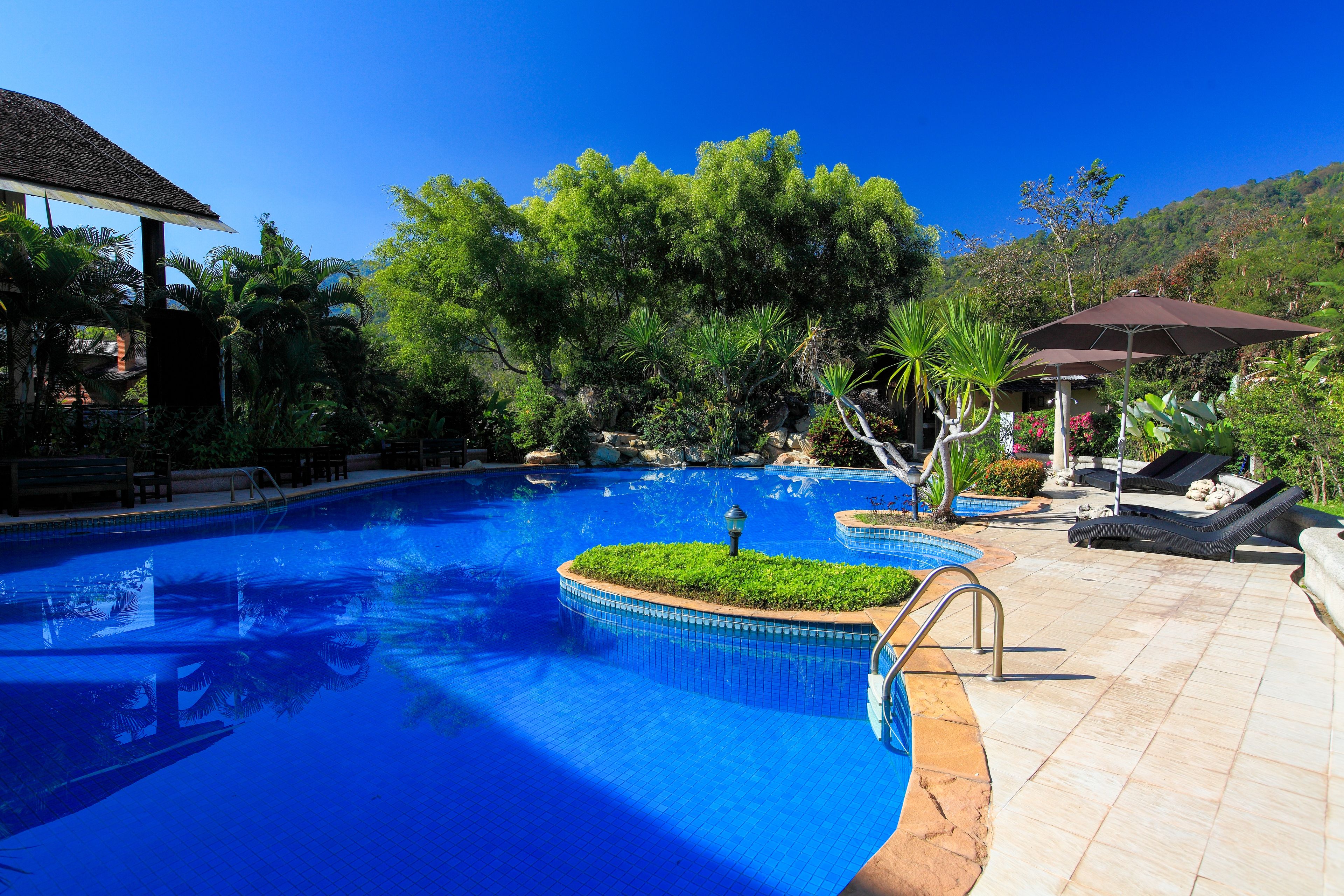 Piscina com deck revestido, espreguiçadeiras e um gazebo.