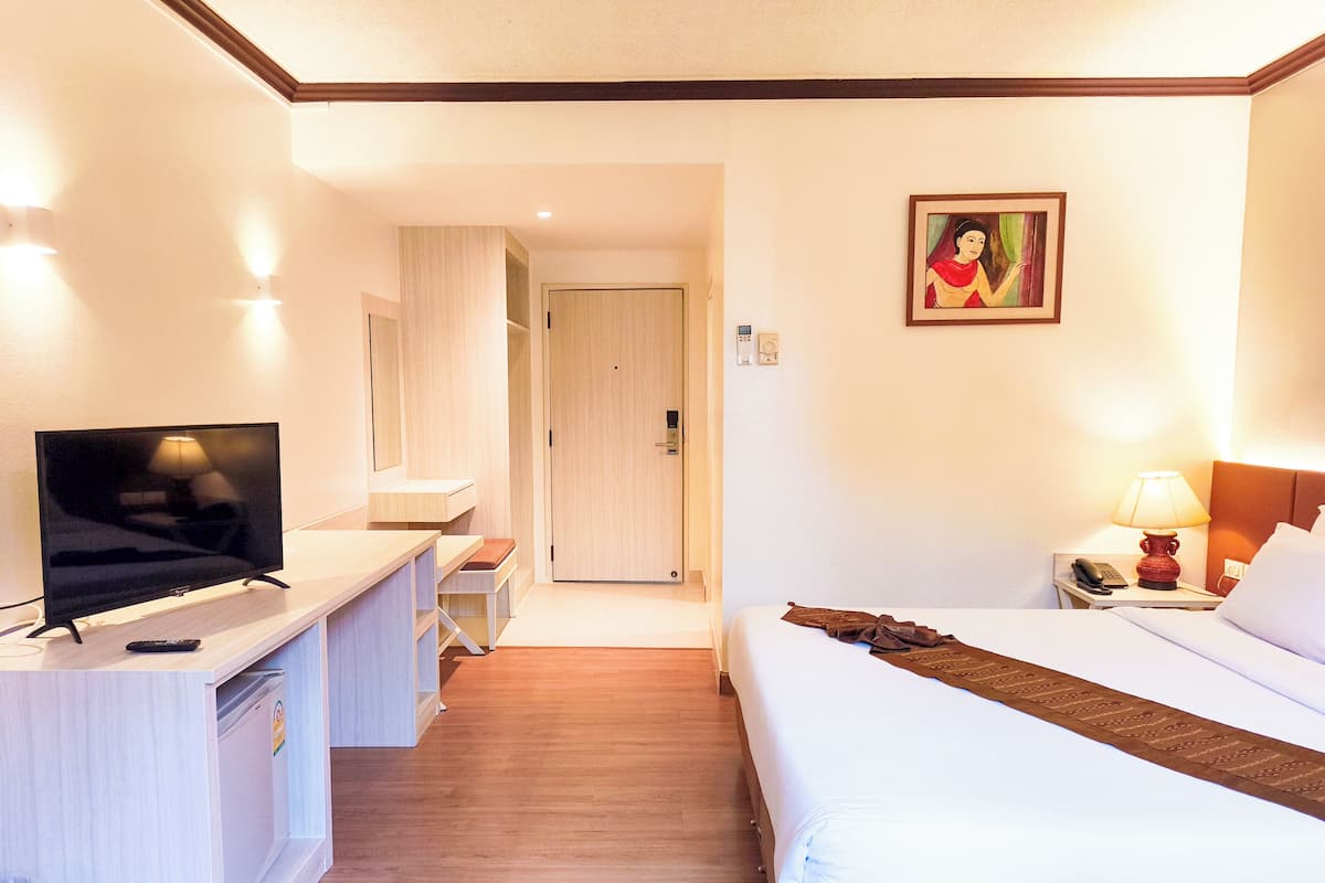 Quarto de hotel com televisão, escrivaninha, cama, abajur e um quadro na parede.
