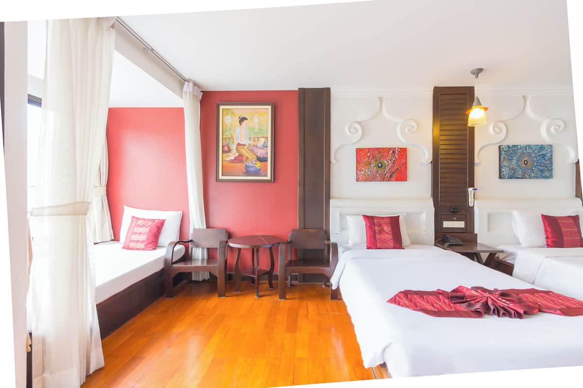 Quarto de hotel com duas camas, uma mesa de jantar e cadeiras. Há quadros nas paredes e uma janela com cortinas.