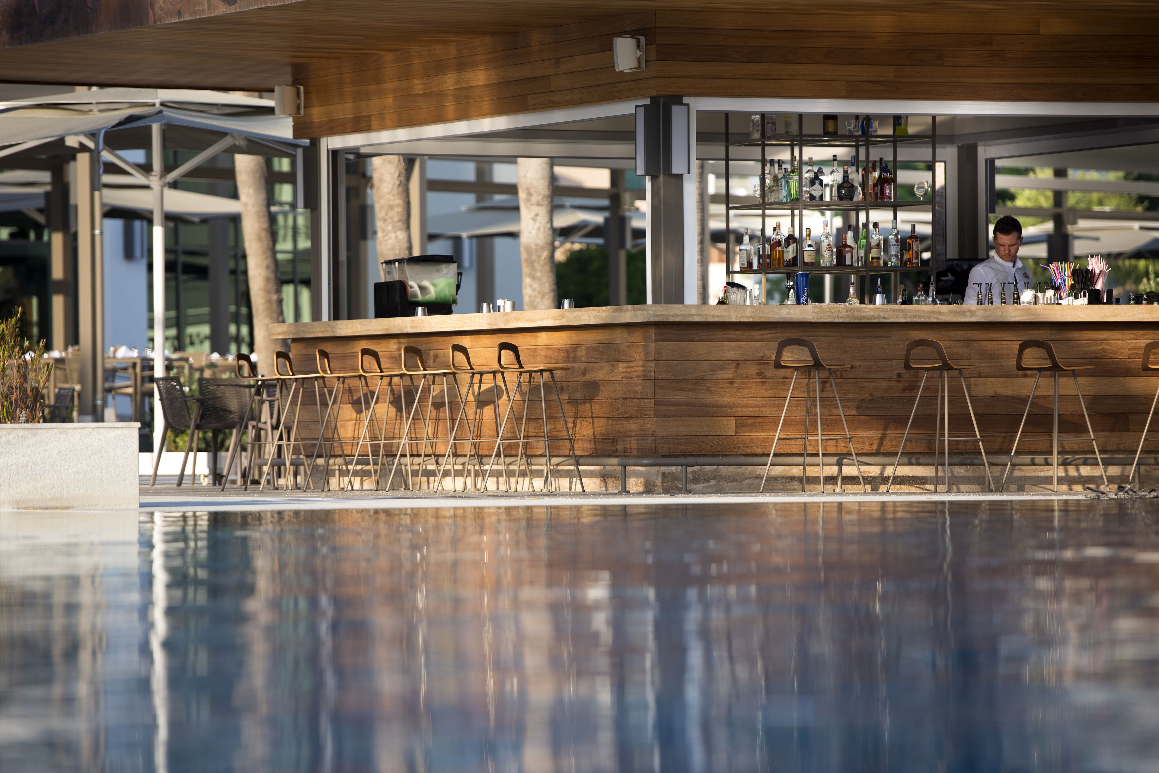 Zona de bar com piscina, balcão de madeira e cadeiras.