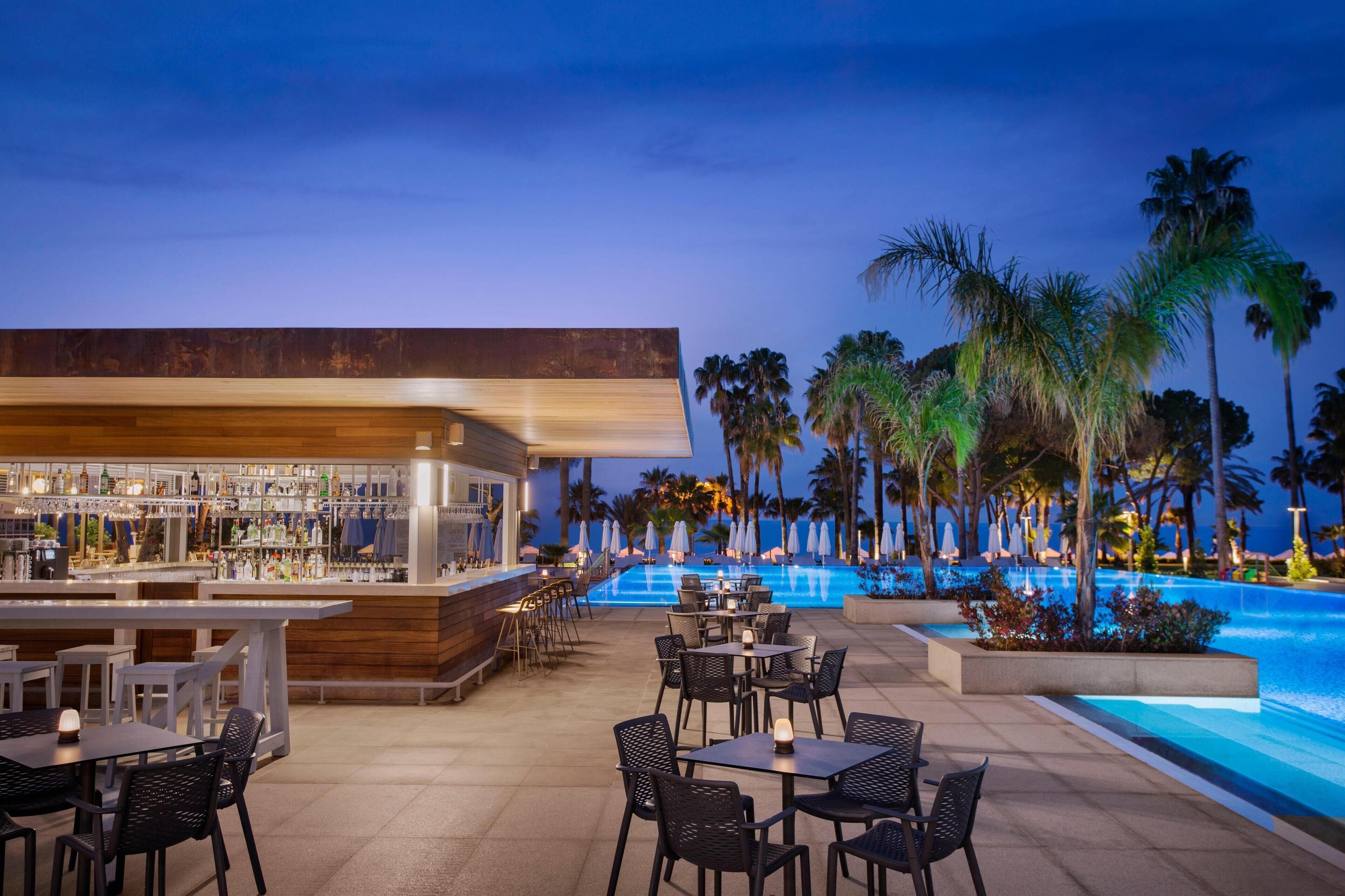 Uma área de bar ao ar livre com piscina e palmeiras.