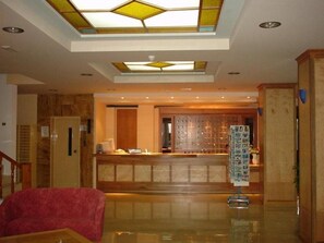 Um hall de hotel com uma mesa de recepção, um sofá vermelho e uma mesa de centro de vidro.