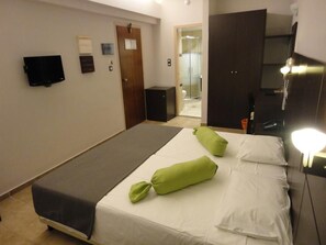Quarto de hotel com cama, televisão, porta e banheiro visível por uma porta aberta.