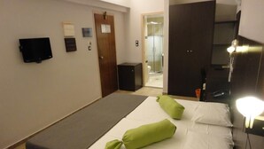 Quarto de hotel com cama, televisão, porta e banheiro visível por uma porta aberta.