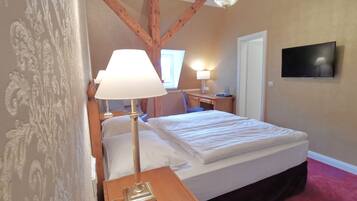 Quarto de hotel com cama, mesas de cabeceira, escrivaninha, cadeira, televisão e lustre.