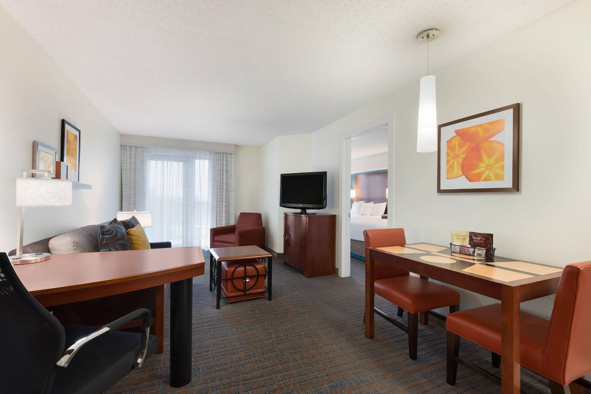 Quarto de hotel com área de jantar, televisão, sofá e cama.