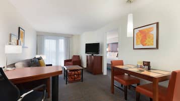 Quarto de hotel com área de jantar, televisão, sofá e cama.