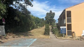 Uma área de estacionamento com vagas azuis para deficientes, um edifício com a placa indicando 'Campanile' e 'Côte Collines', e um céu limpo.