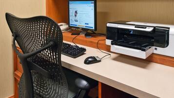 Uma mesa com um computador, uma impressora, um teclado, um rato e uma cadeira de escritório vazada.