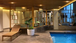 Uma área interna de piscina moderna com um banco de madeira, uma planta em vaso e vista para a academia ao fundo.