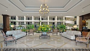 Um hall amplo com lustre, sofás e um arranjo floral central.