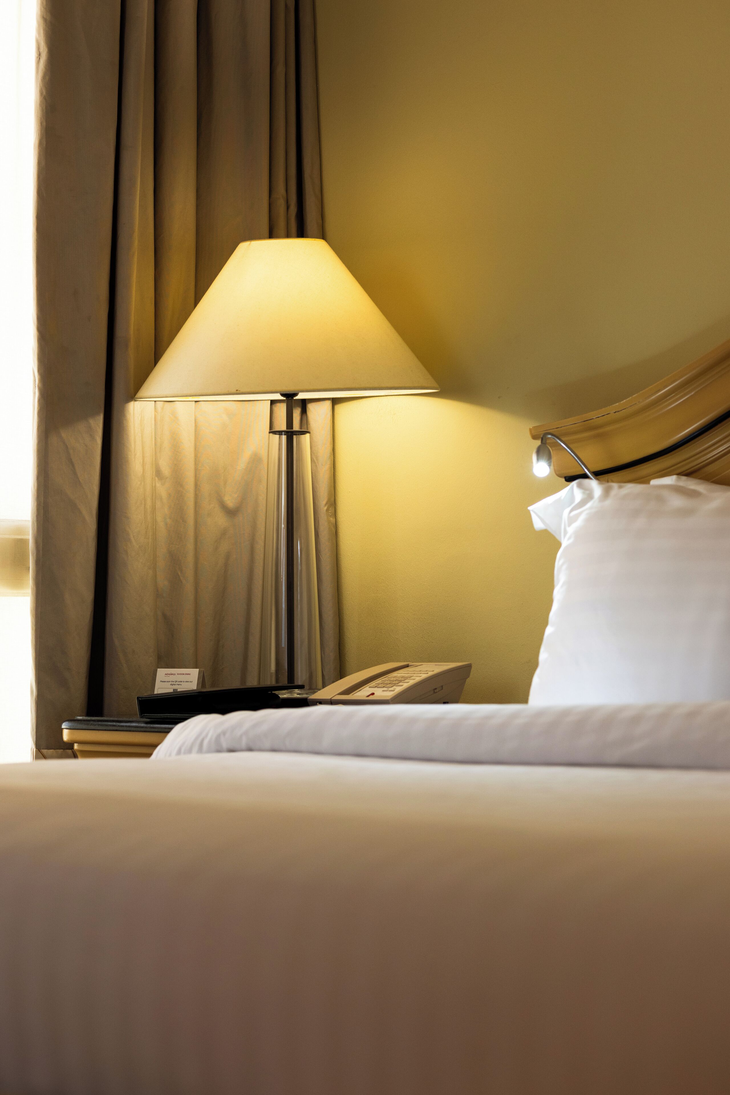 Quarto de hotel com cama, mesa de cabeceira e cortinas.