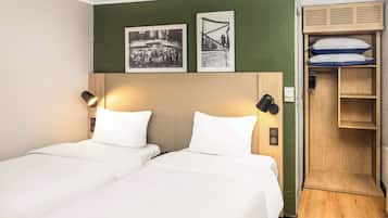 Quarto de hotel com duas camas, um guarda-roupa de madeira e duas molduras na parede.