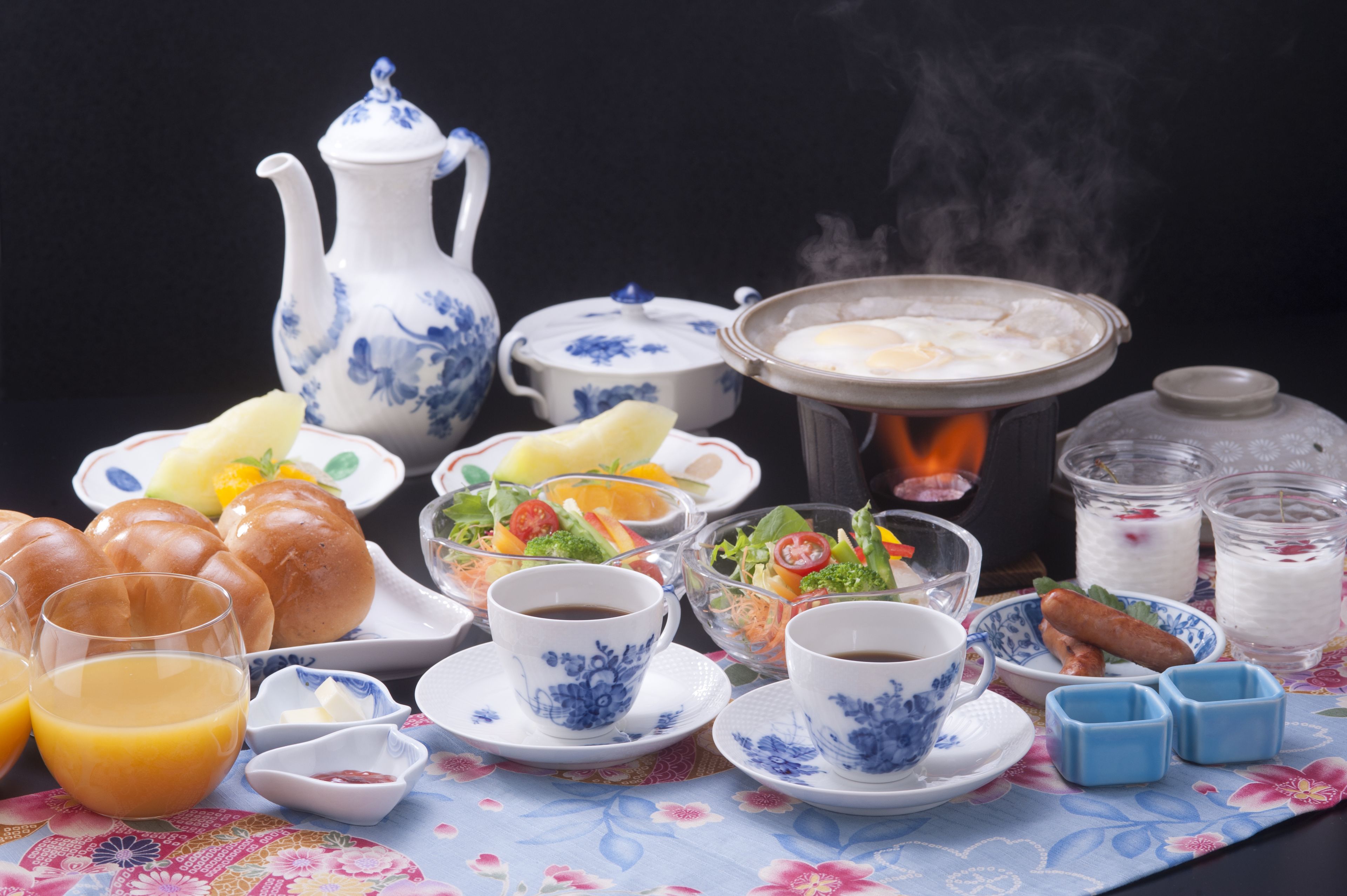 Mesa posta com itens de café da manhã, incluindo pão, frutas, café e uma chaleira.
