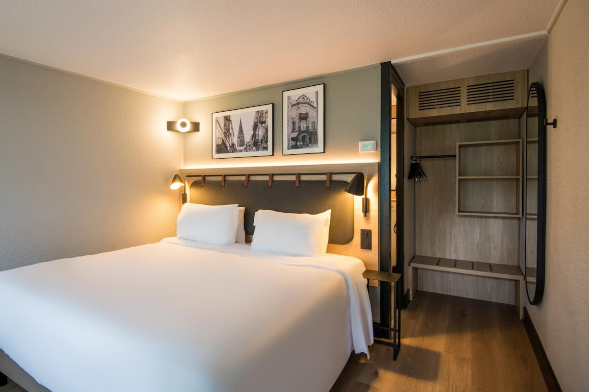Quarto de hotel com uma cama grande, televisão presa na parede e guarda-roupa de madeira.