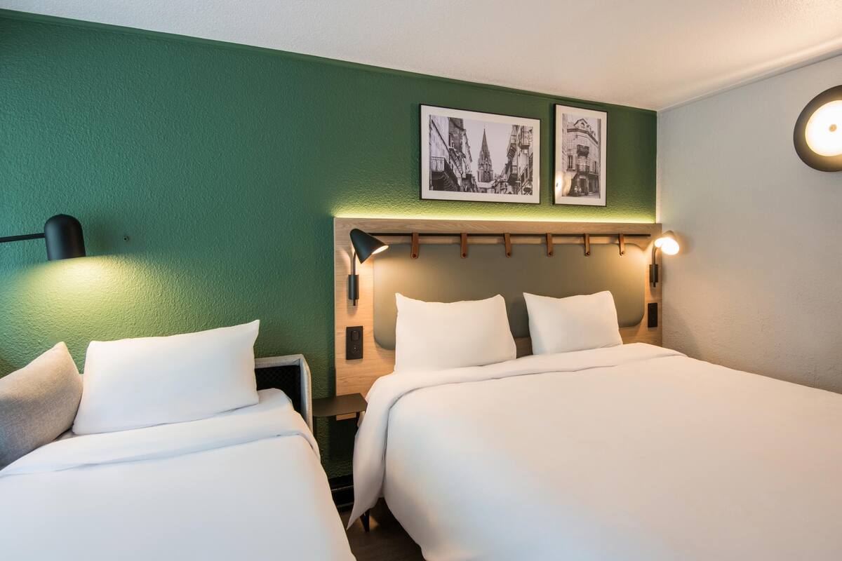 Quarto de hotel com duas camas, uma parede verde e duas fotografias em preto e branco.