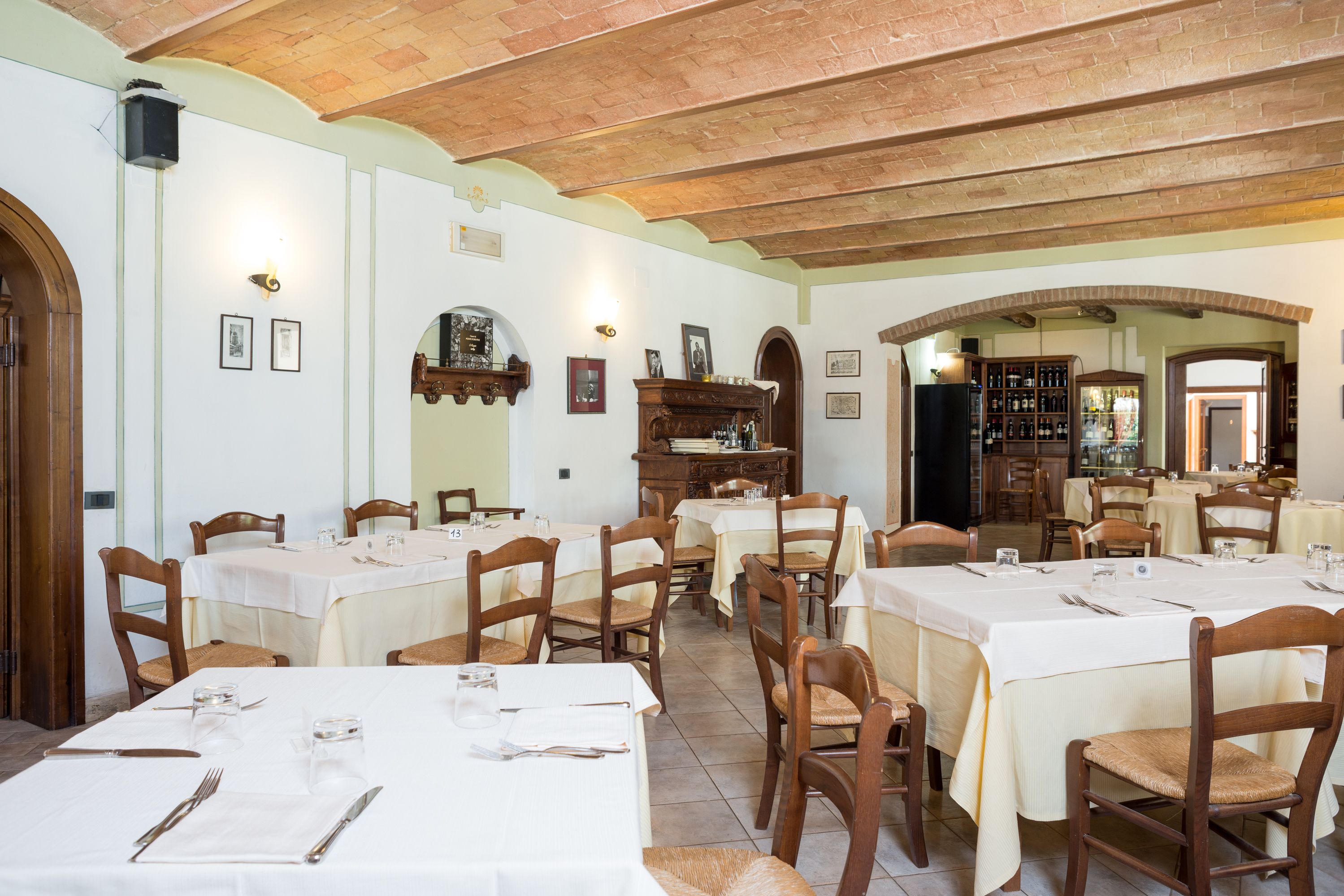 Restaurante com várias mesas preparadas para refeições, cadeiras de madeira e teto de tijolos.