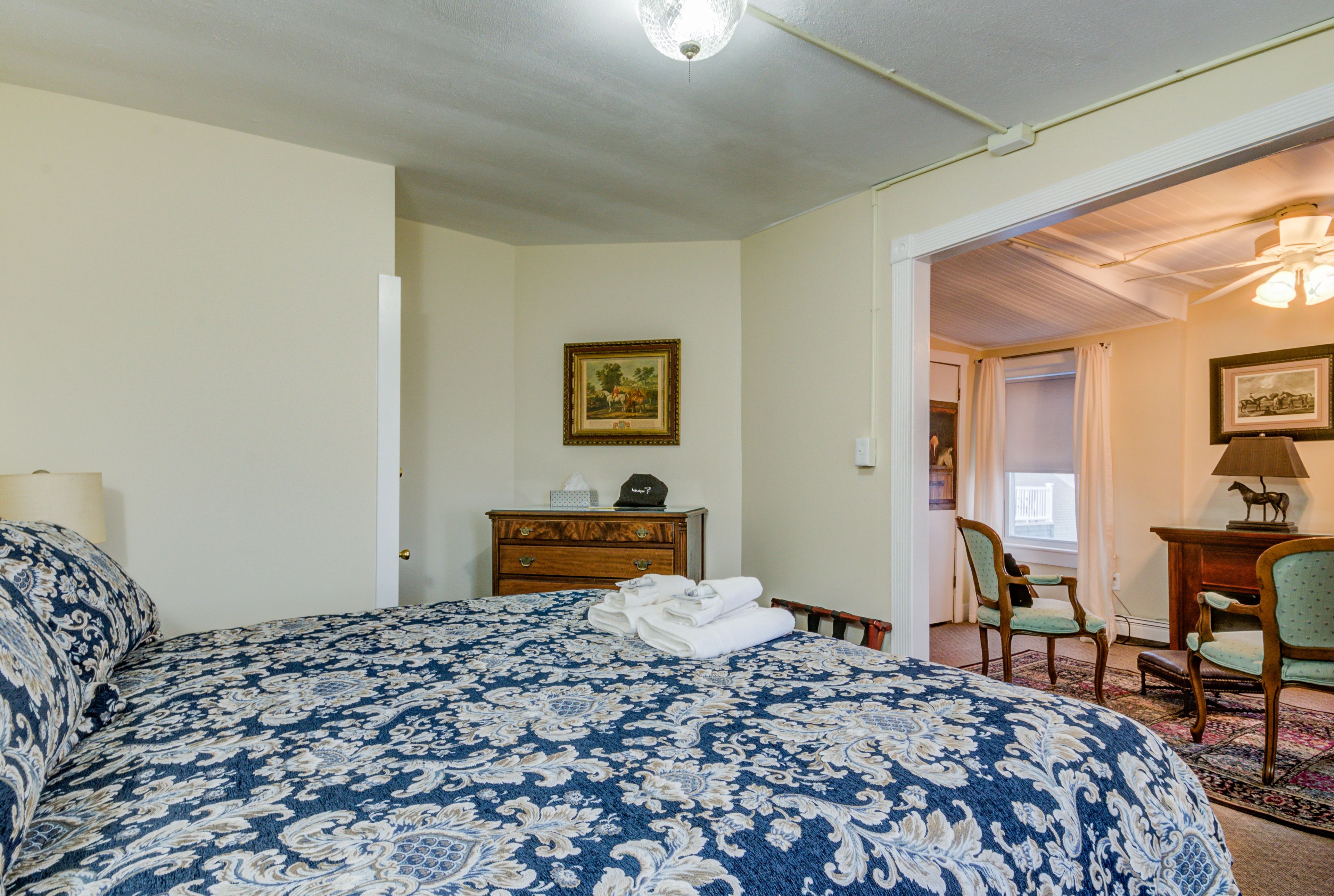 Quarto com uma cama grande, cômoda, cadeira e escrivaninha com abajur.