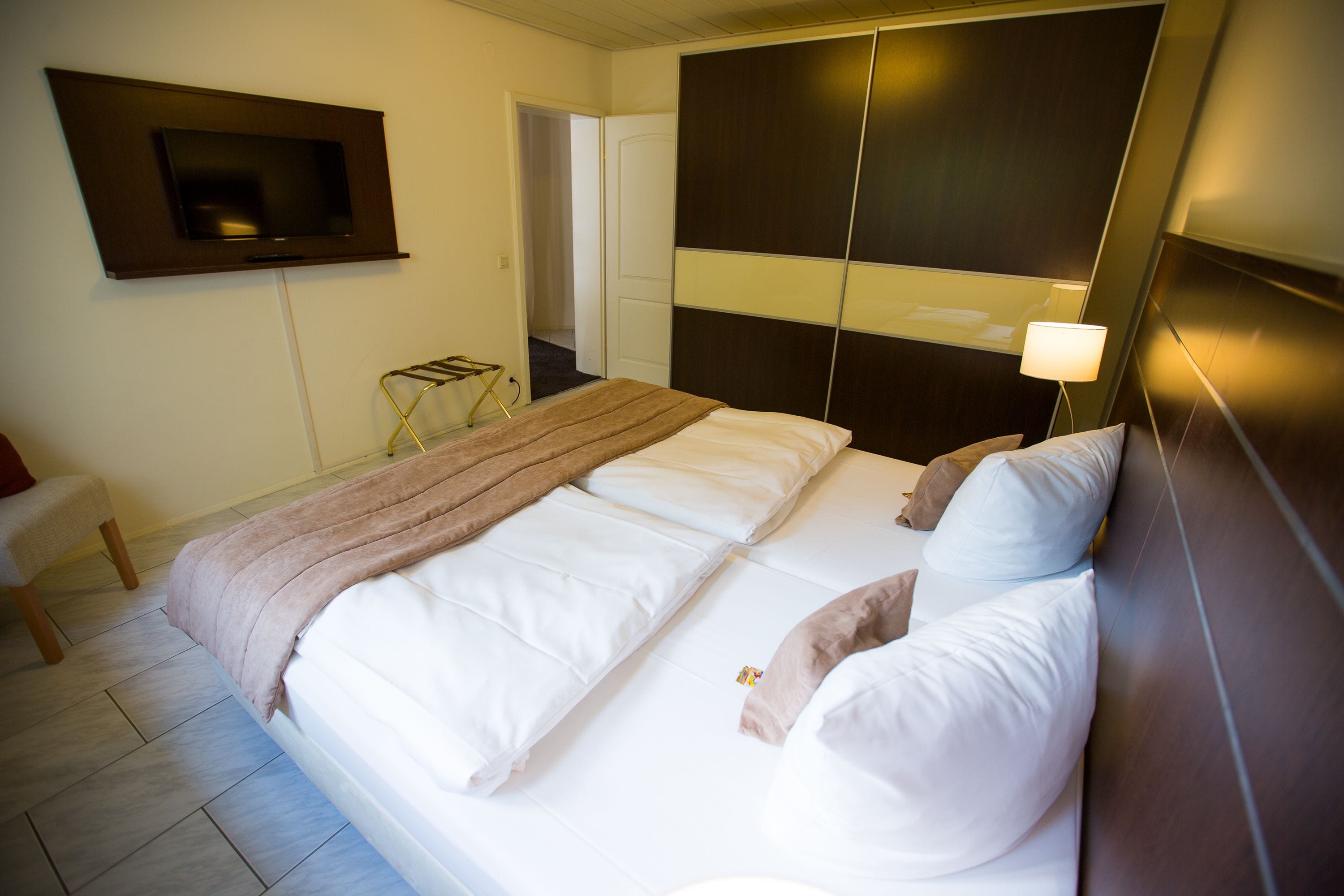 Quarto de hotel com cama, televisão presa na parede e abajur.