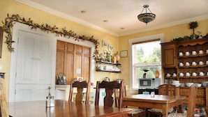 Uma sala de jantar com mesa e cadeiras de madeira, uma cozinha com armários e micro-ondas, e uma janela com persianas.