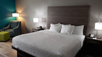 Quarto de hotel com uma cama grande, duas luminárias de cabeceira, uma cadeira, uma mesinha e um telefone no criado-mudo.