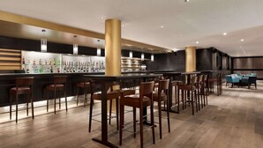 Uma área de bar com banquetas altas, balcão e um espaço para sentar com mesas e cadeiras.