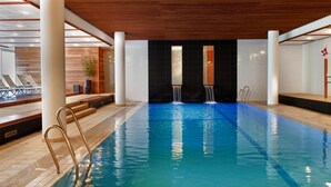 Piscina com teto de madeira, colunas brancas e uma cascata.