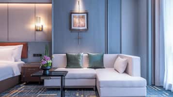 Quarto de hotel moderno com cama, sofá, mesa pequena e um objeto decorativo na parede.