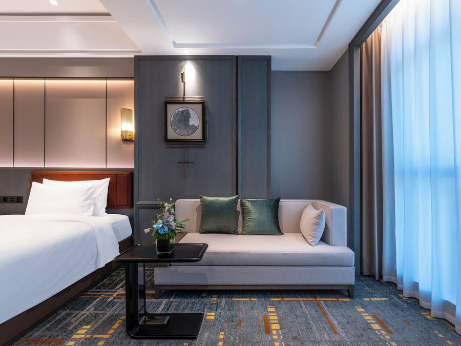 Quarto de hotel com cama, sofá, uma mesa pequena e uma obra de arte na parede.