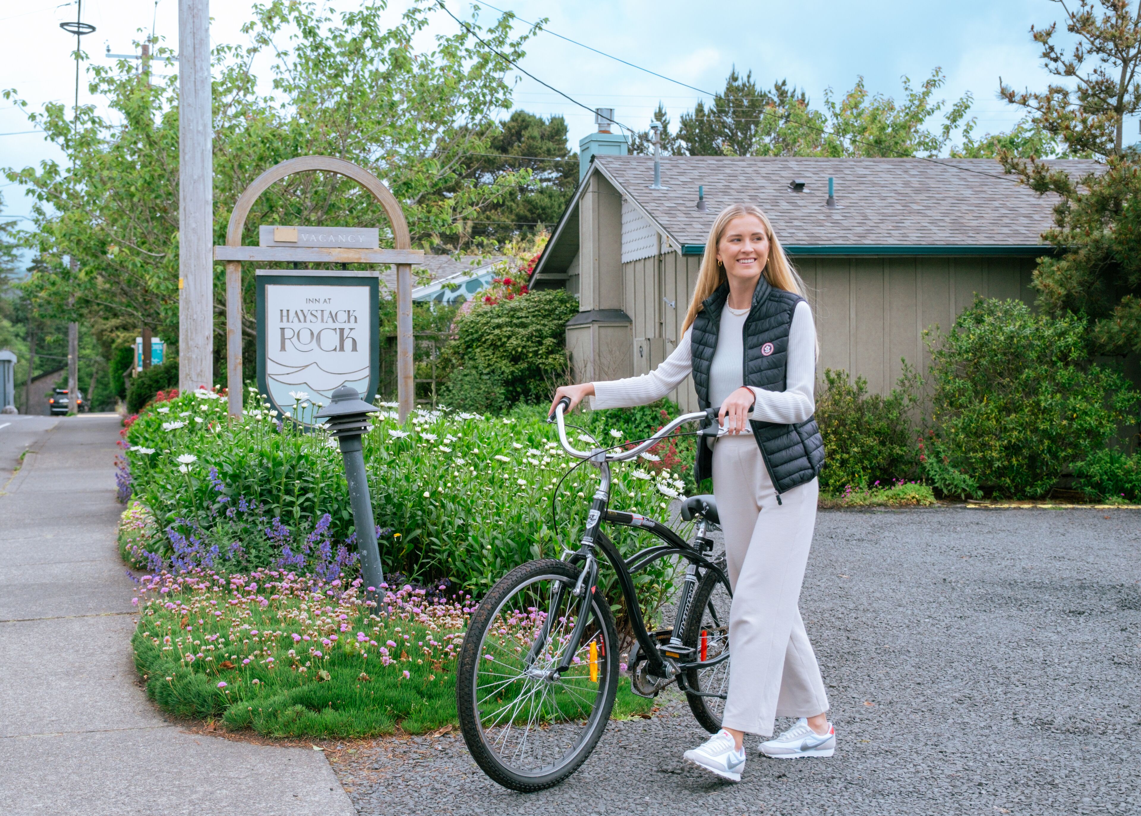 Placa do Haystack Rock Inn, uma bicicleta estacionada na frente e uma mulher segurando o guidão.