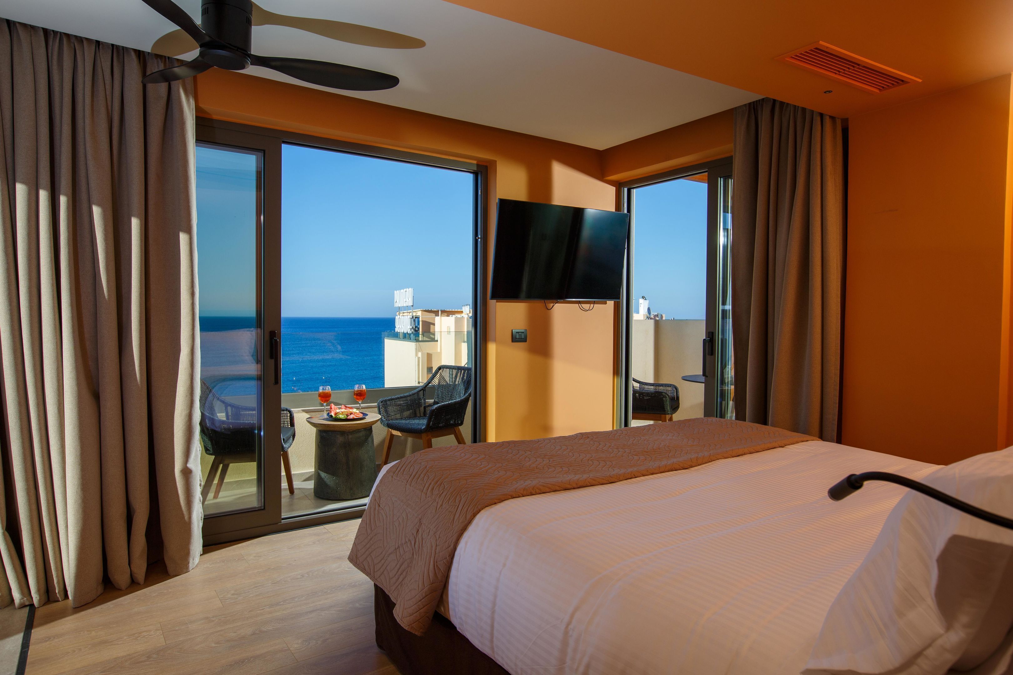 Quarto de hotel com cama, televisão e varanda com vista para o mar.