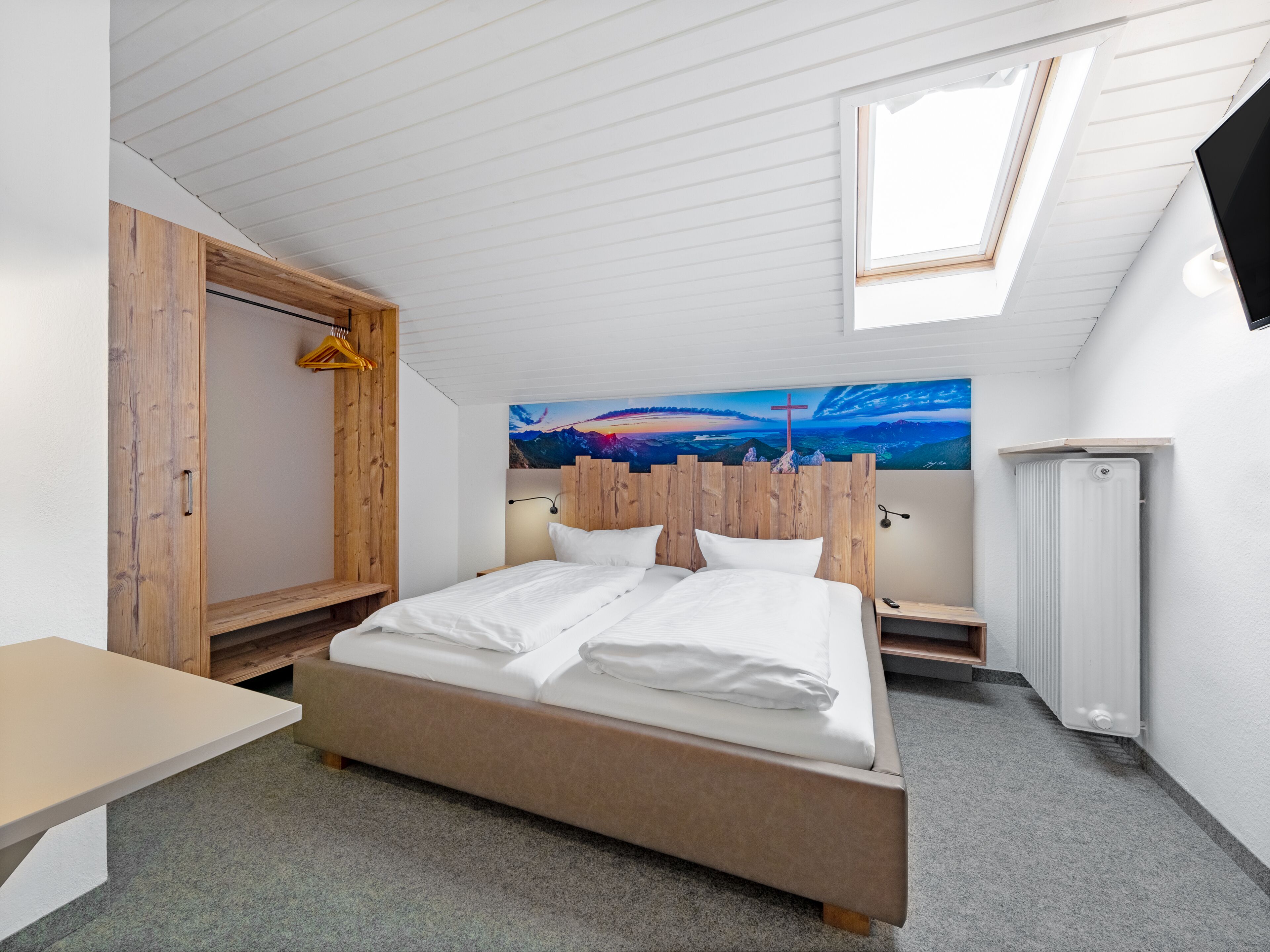 Quarto com cama, guarda-roupa de madeira, radiador e um quadro de paisagem.