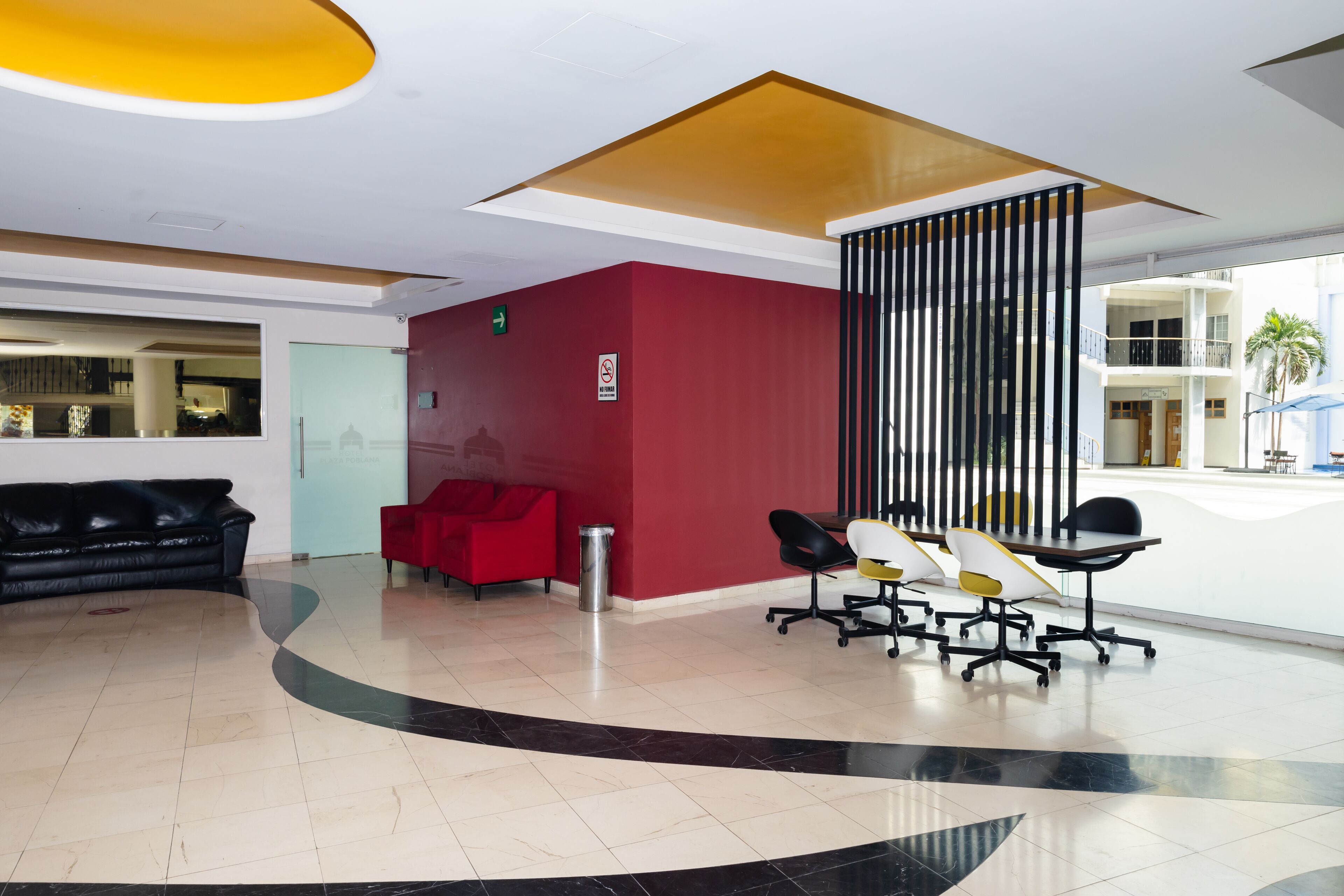 Um hall moderno com piso em preto e branco curvo, paredes vermelhas e teto amarelo. Há sofás de couro preto, um sofá vermelho e uma mesa com cadeiras.