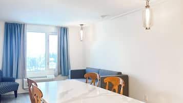 Uma sala de jantar com uma mesa branca, cadeiras de madeira, um sofá azul e duas luminárias pendentes.