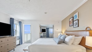 Quarto de hotel com uma cama grande, televisão, penteadeira e varanda com vista.