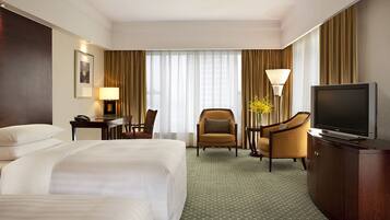 Quarto de hotel com duas camas, uma secretária com luminária, televisão e uma cadeira.