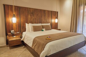 Quarto de hotel com cabeceira de madeira, cama com roupa de cama branca e detalhes em castanho, mesa de cabeceira com telefone e criado-mudo.