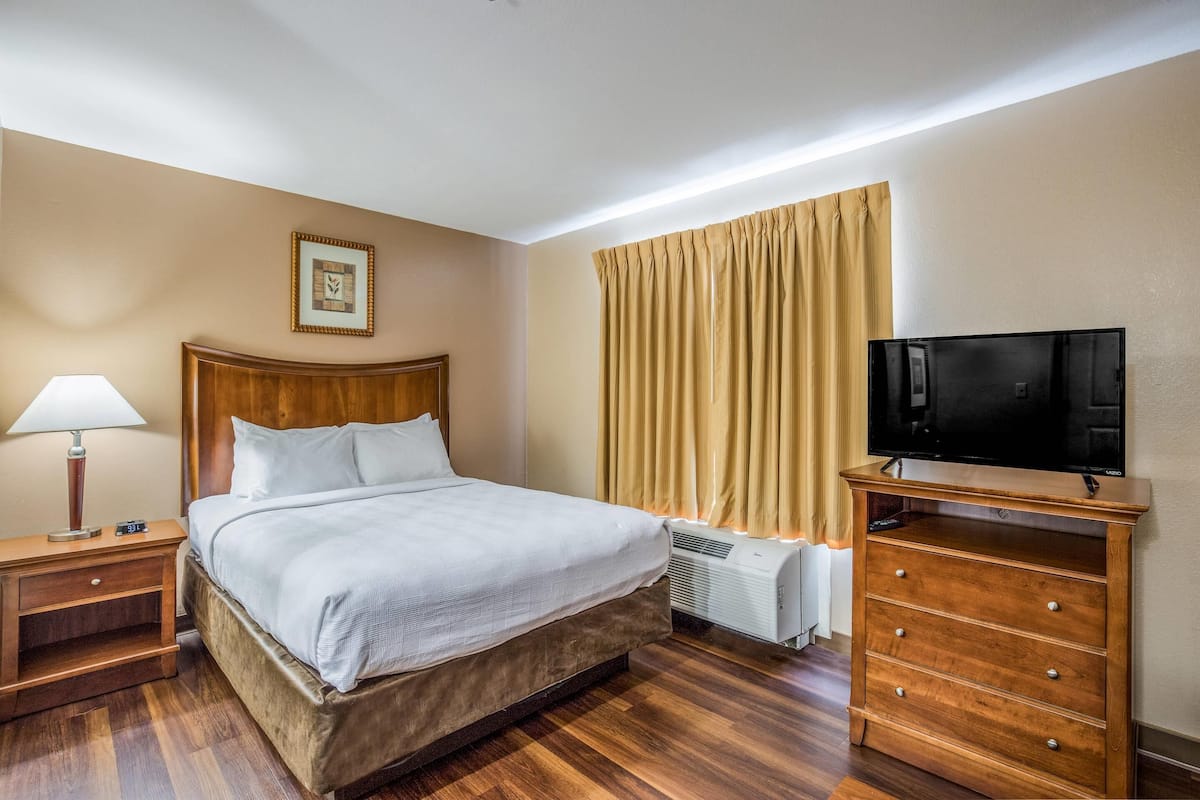 Quarto de hotel com cama, mesa de cabeceira, abajur, televisão, cômoda e cortinas.
