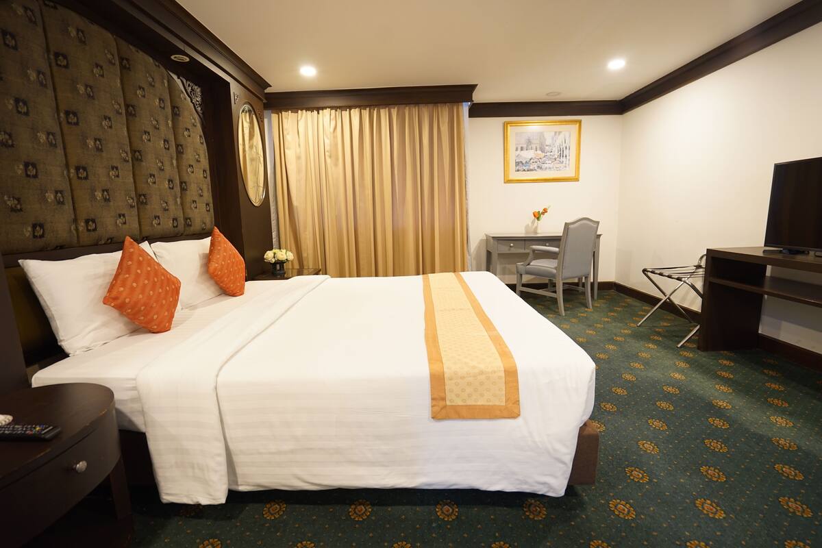 Quarto de hotel com uma cama grande, uma escrivaninha, uma cadeira e uma televisão.