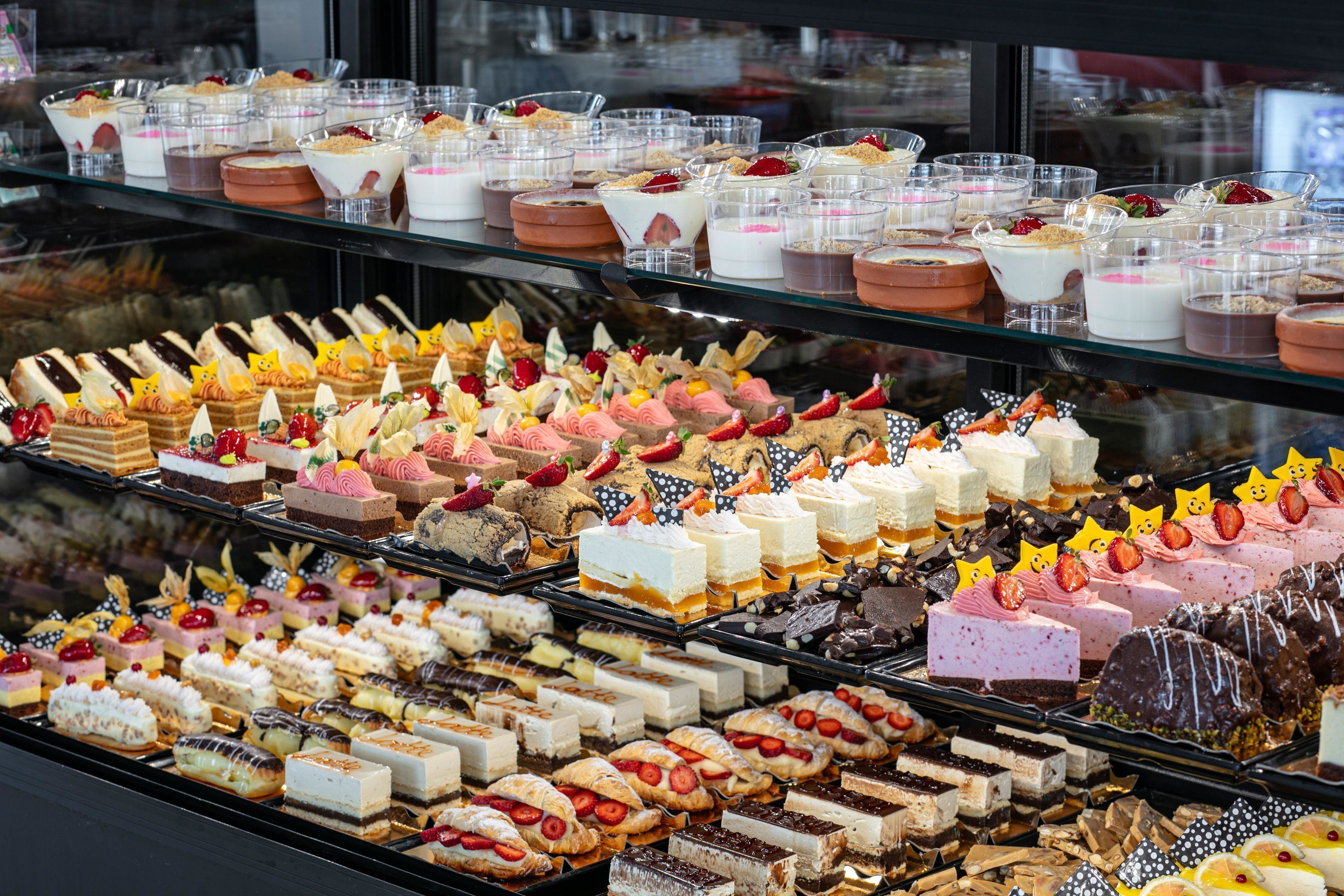 Diversos doces expostos em uma vitrine de vidro, incluindo bolos, doces e outras guloseimas.